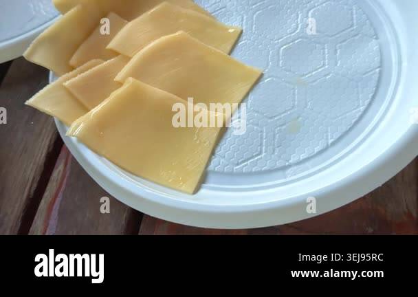 Hands placing sliced hard cheese cubes onto disposable plate during ...
