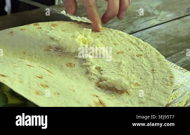 Homemade lavash snack preparation with creamy soft cheese being spread ...
