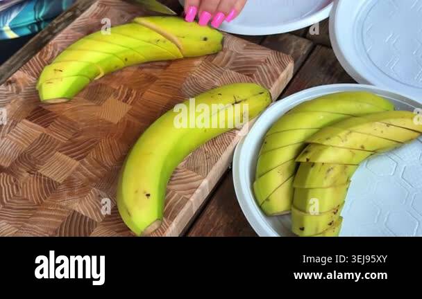 Female hands cutting peeled greenish banana into small slices on wooden ...