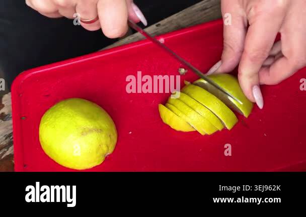 Woman slicing fresh lemon and lime on red cutting board during citrus ...