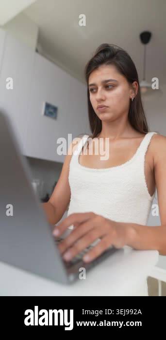 Focused woman typing on laptop kitchen counter, natural light, modern ...