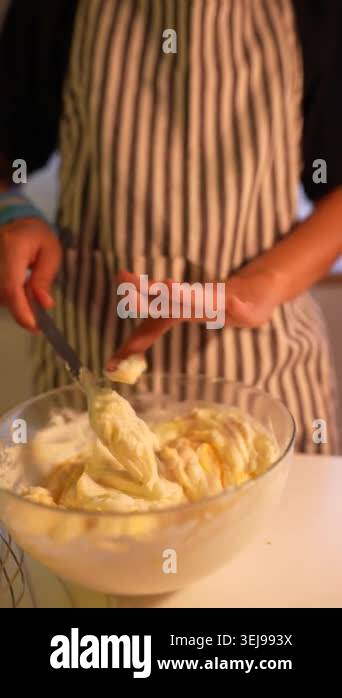 Woman folding batter with fork in glass bowl, striped apron, gentle ...