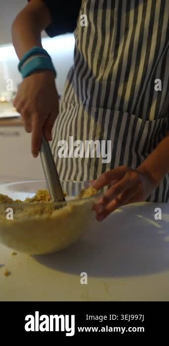 Closeup hands mashing dough in glass bowl, striped apron, blue ...