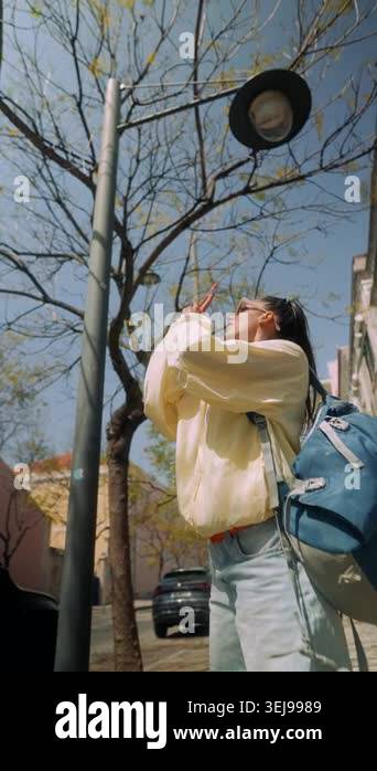 White woman posing with blue backpack on sunlit street, leaning into ...