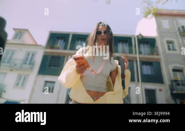 Young woman scanning phone for directions on sunny square, yellow ...