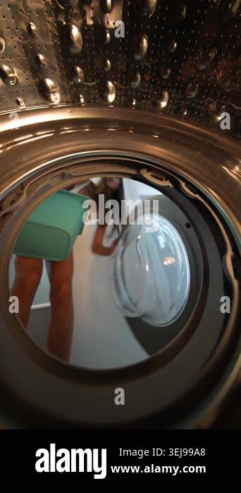 Inside washer drum woman loads clothes and closes door, cinematic low ...