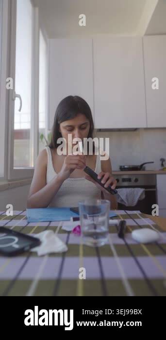 Young woman testing glucose at table focused on lancet and meter, quiet ...