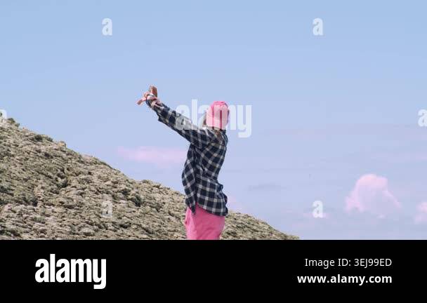 Young woman filming seaside on rocky shore in pink outfit, smartphone ...