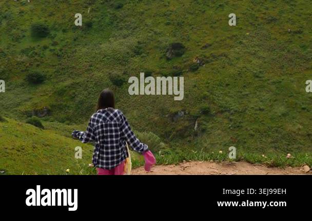 Young woman walking with outstretched arms on green slope, checkered ...