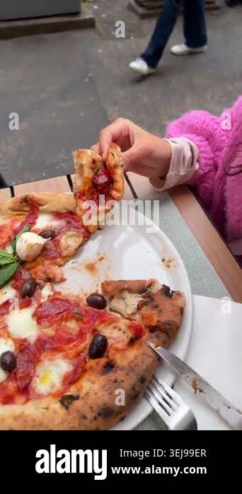 Closeup hand lifting pizza slice outdoor bistro, pink sleeve visible ...
