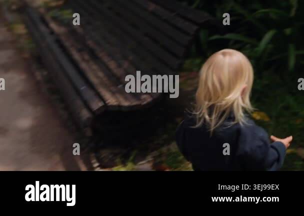 White toddler walking past bench, blonde child holding leaf, slow steps ...