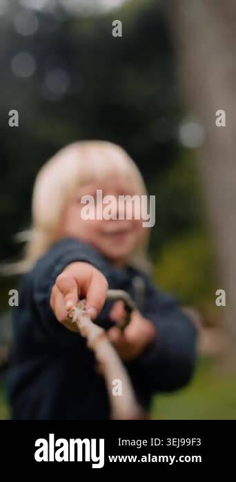 Toddler pulling stick in park, playful tug motion and focused face ...