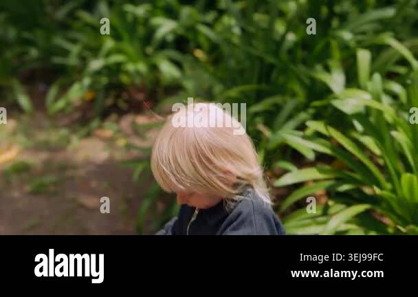 White toddler exploring lush green plants, blonde child bending toward ...