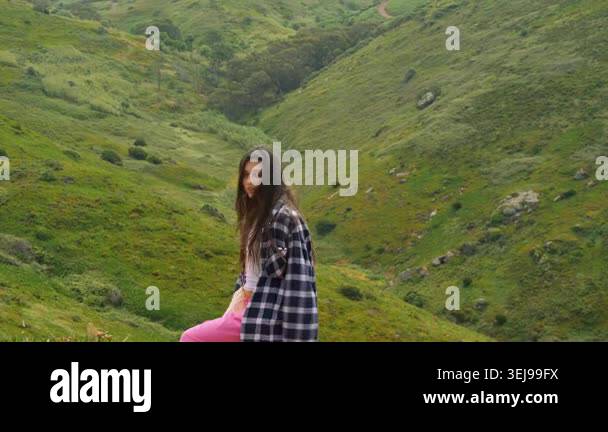 Young woman exploring grassy hilltop pausing at overlook, holding light ...