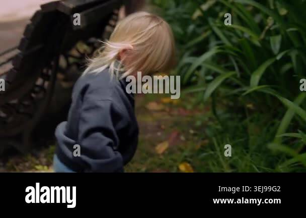 White toddler inspecting plants near bench, blonde child crouching ...