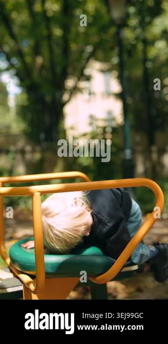 Blonde white toddler on playground carousel, sunlit park setting with ...