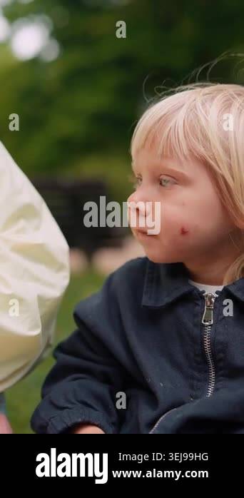 Toddler looking sideways in park, curious gaze and small cheek scratch ...