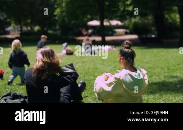 Two white women sitting on grass, sharing coffee and notes, backpacks ...