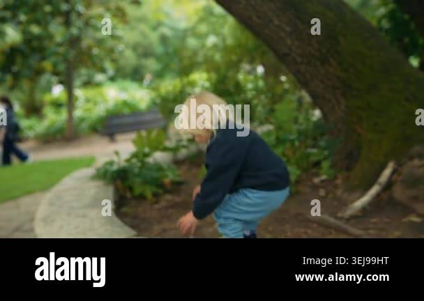 Blonde white toddler exploring park pathway, wandering along stone path ...