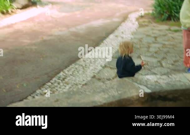 Blonde caucasian toddler reaching for caregiver on cobblestone path ...