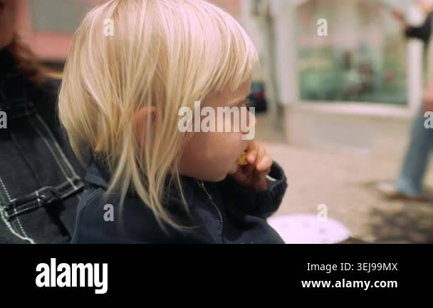 Blond toddler eating snack at cafe, thoughtful profile in soft ...