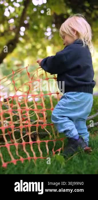 White toddler navigating orange safety fence park, climbing small ...