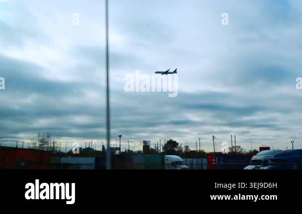 Plane flies over the cityscape against dramatic sky. Footage from a car ...