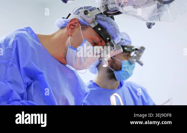 Two male medics in surgical loupes and blue robes. Professionals work ...