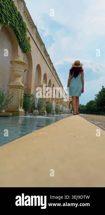 Woman Walking Beside Formal Garden Fountain Arcade. Rear view of woman ...