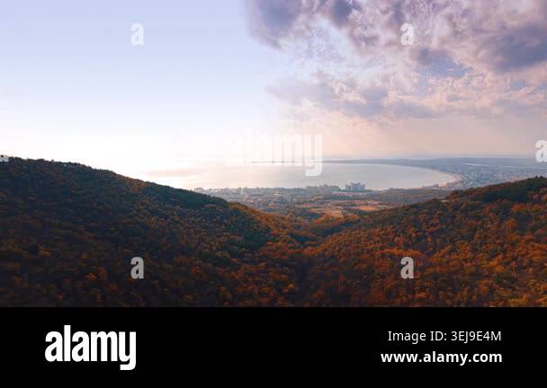 Aerial mountain valley view of autumn forest hills framing coastal city ...