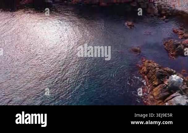 Aerial view of sheltered rocky cove with sun-reflected water and pebble ...