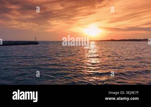 Sunset over open sea with stone pier bird silhouette and orange sky ...