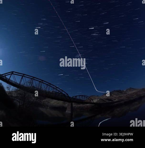 Dark night sky glows with a bright moon. Star trails swirl across the ...