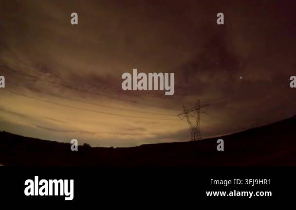 Dark evening sky with wispy clouds and horizontal power lines. Lone ...