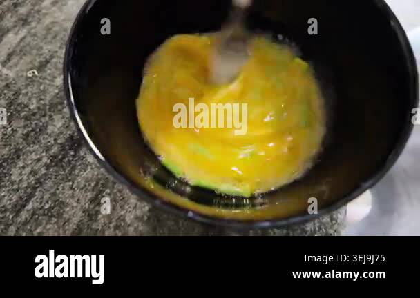 Female hands holding a black bowl and whisking fresh eggs with a fork ...
