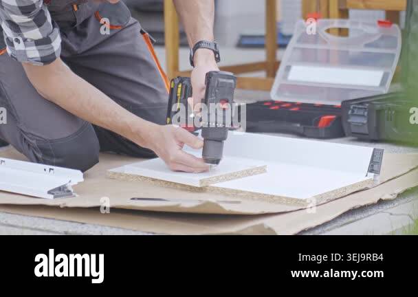 Man drills holes in drawer panel with cordless drill on cardboard ...