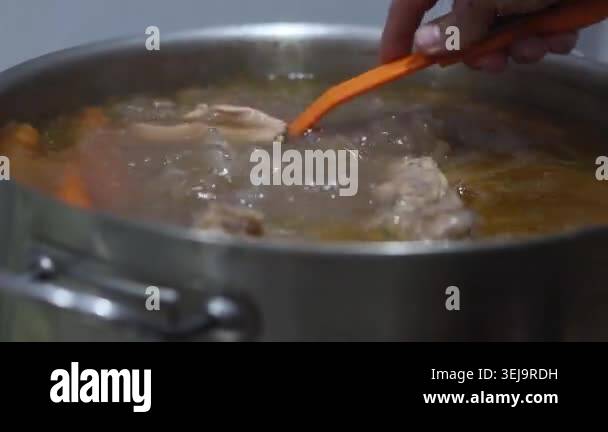 Professional chef preparing a hearty beef stew, skimming scum from the ...