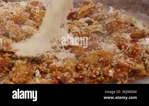 Close-up of a person pouring and mixing rice into a traditional spanish ...