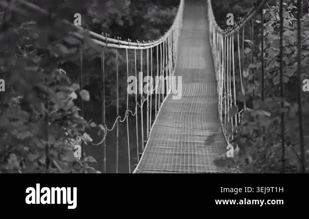 A black and white shot of a long suspension footbridge stretching ...