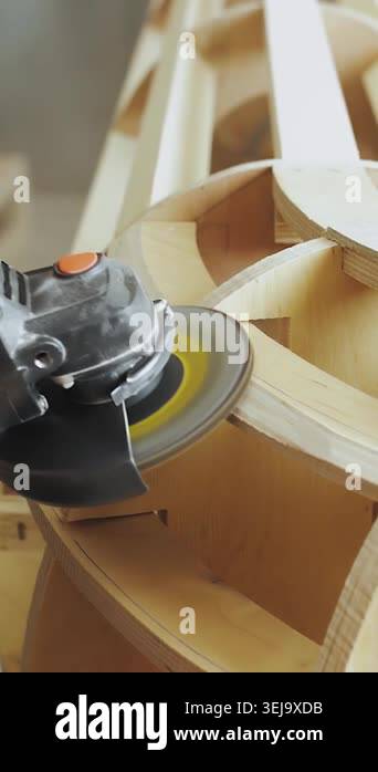 Vertical video. Carpenter grinding curved wooden furniture part with ...