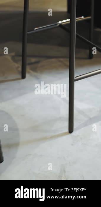 Vertical video. Black metal chair frame on polished concrete floor in ...