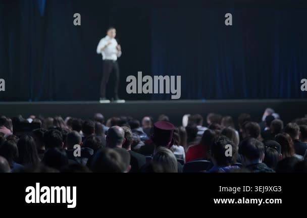 Crowd watching presenter deliver keynote speech on stage at business ...