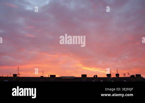 Colors fill the sky as the sun sets behind city buildings and electric ...