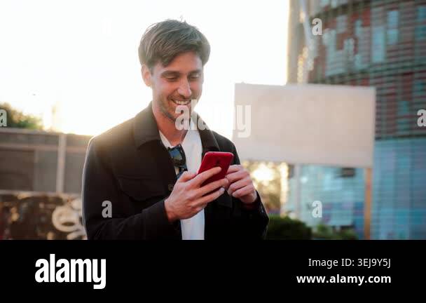 Joyful young man smiling while using smartphone, fully engaged in a ...