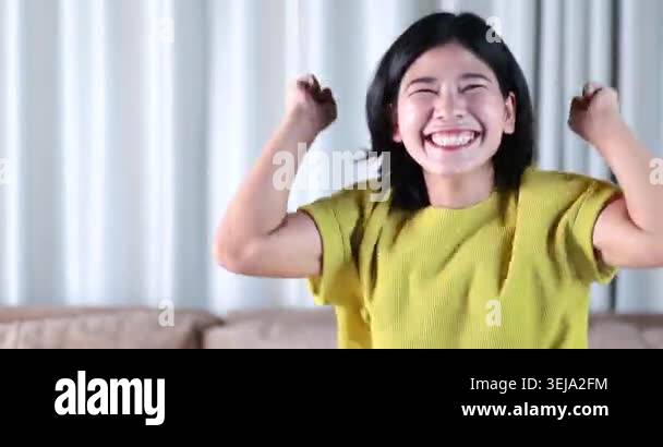 Excited Thai Asian woman celebrating with joy at sofa in home, success ...