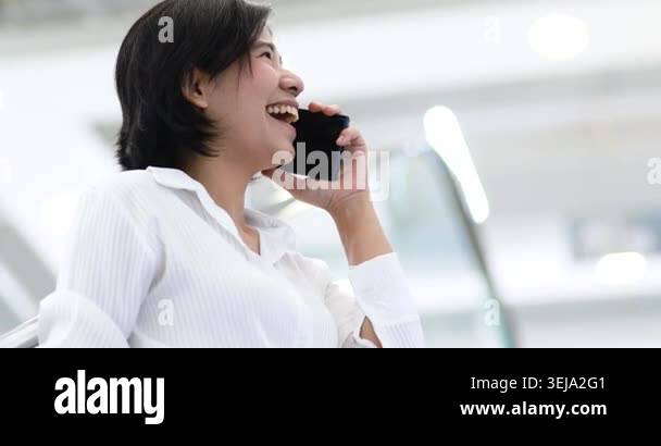 Happy Asian businesswoman talking on smartphone in a modern building ...