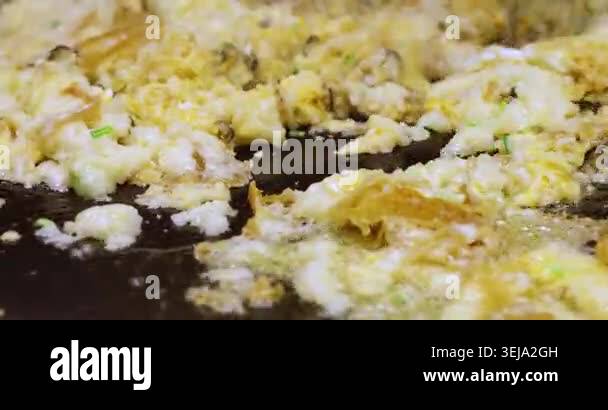 Oyster omelet cooking on a hot pan with metal spatulas. Delicious ...