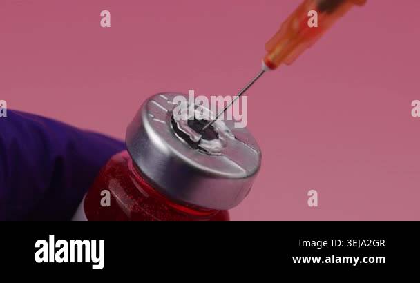 Hand holding a medical glass vial with a syringe needle piercing the ...