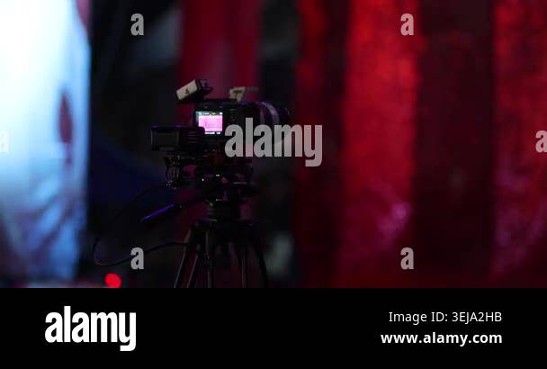 Professional video camera on tripod recording an event with red lights ...