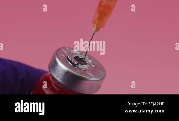 Close view of a human hand holding a drug vial while a syringe needle ...